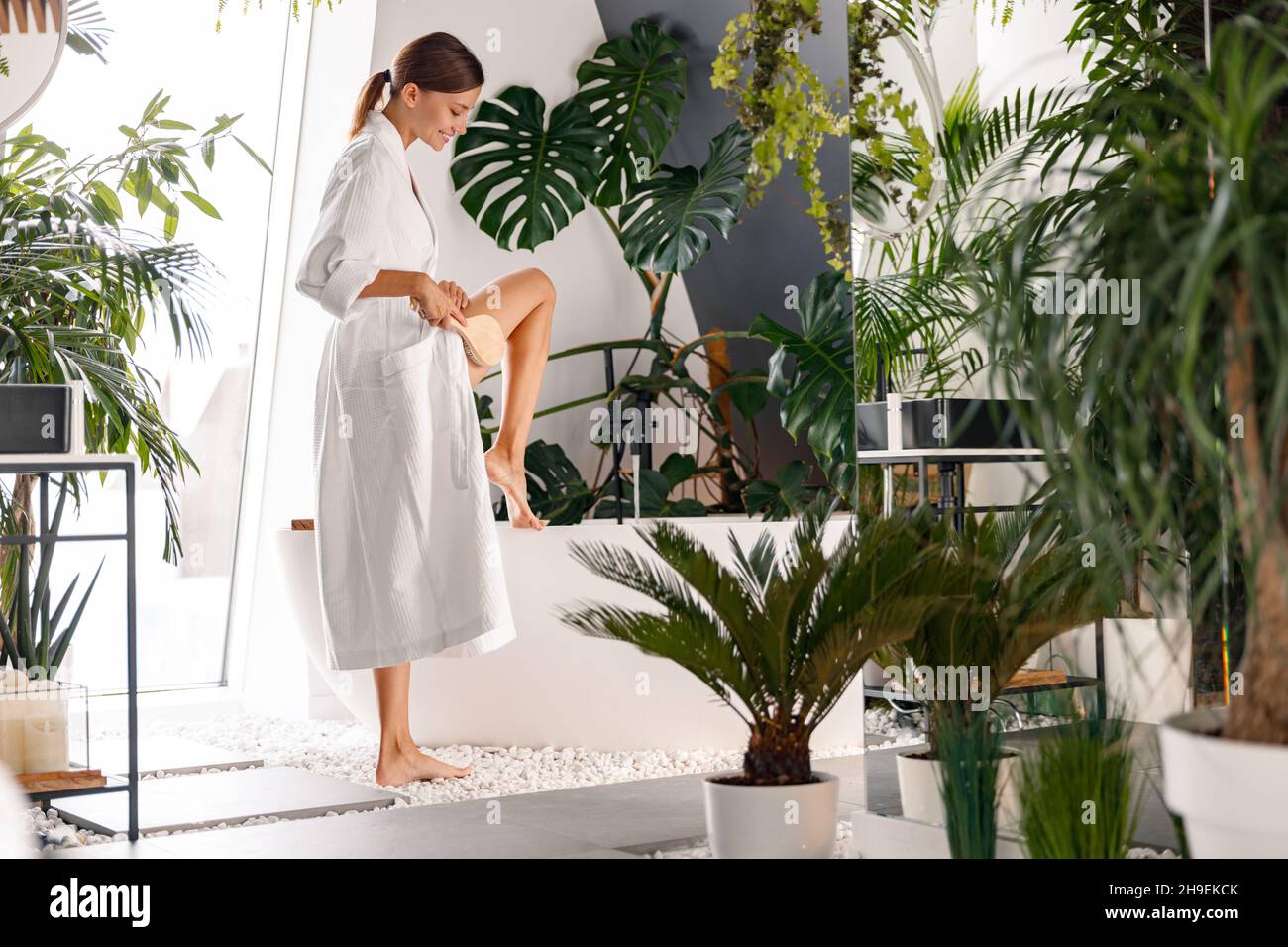Side view of attractive young woman in white bathrobe holding her leg ...