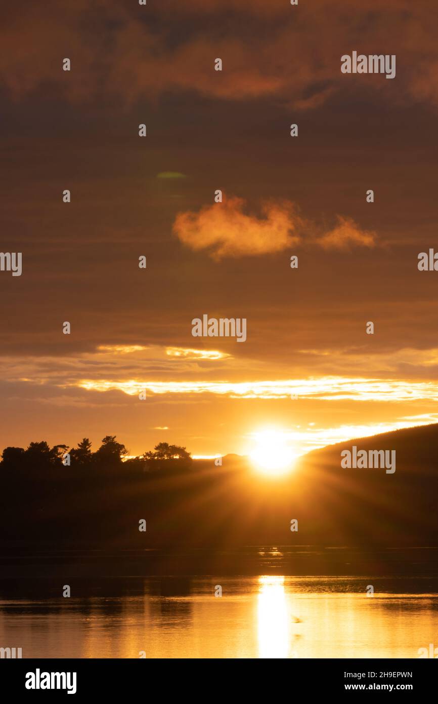 Golden sun rises throwing sunburst effect and silhouetting low hills ...