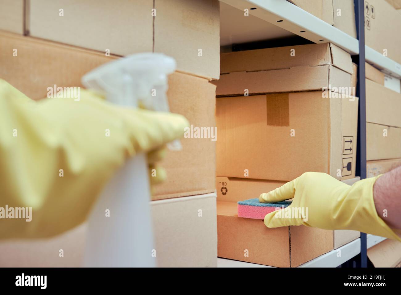 Cleaning in a warehouse, a man in yellow gloves wipes boxes with goods ...