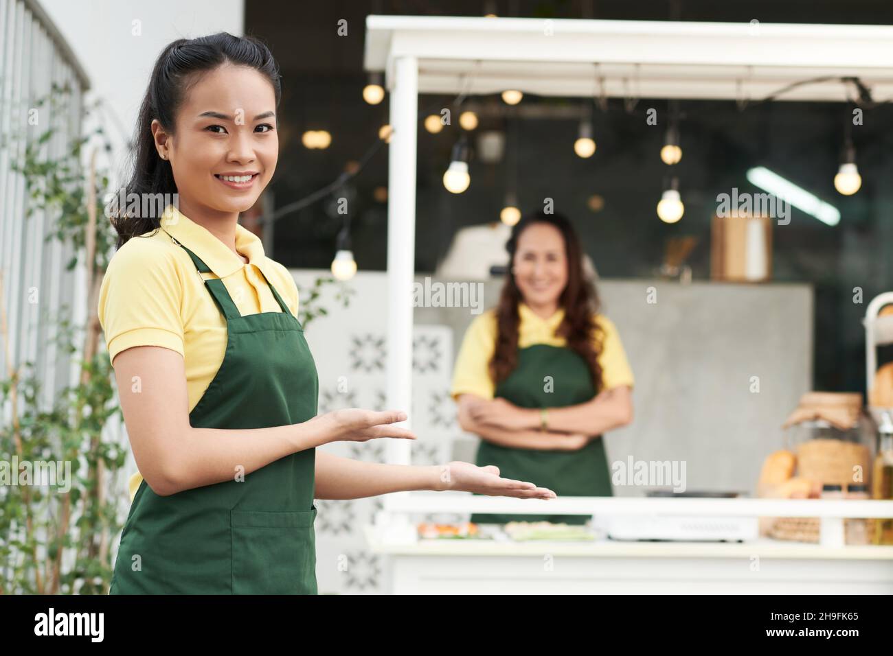 Portrait of smiling young woman welcoming customers to buy sandwich at ...