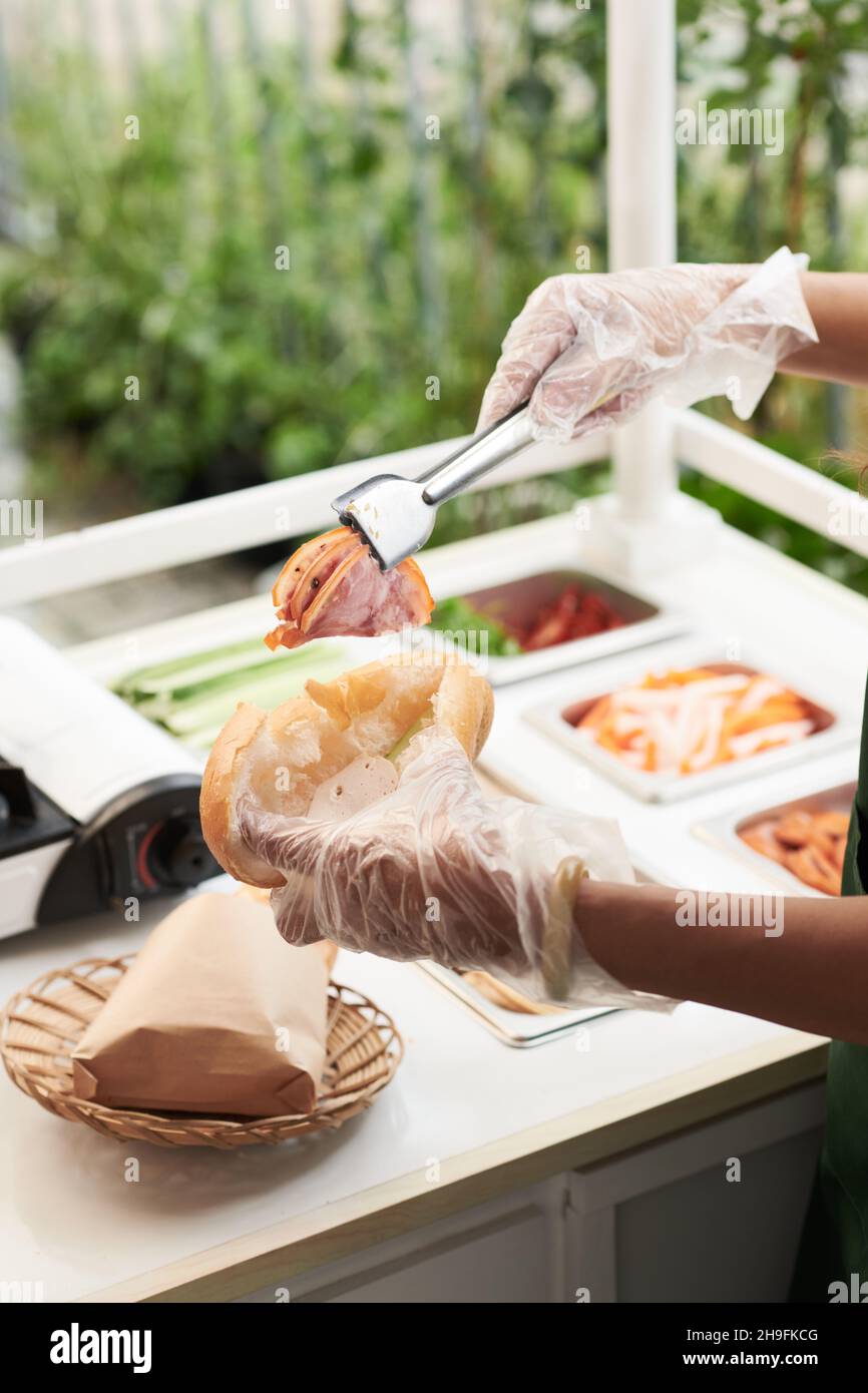 Hands of street food cart vendor adding piece of ham in sandwich for ...
