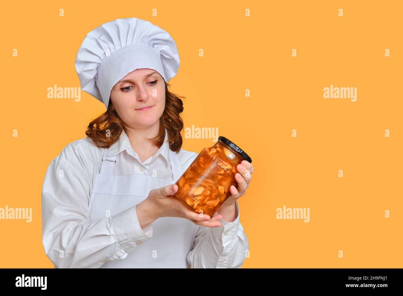 Happy woman chef with jar of fruit jam in hands on studio background ...