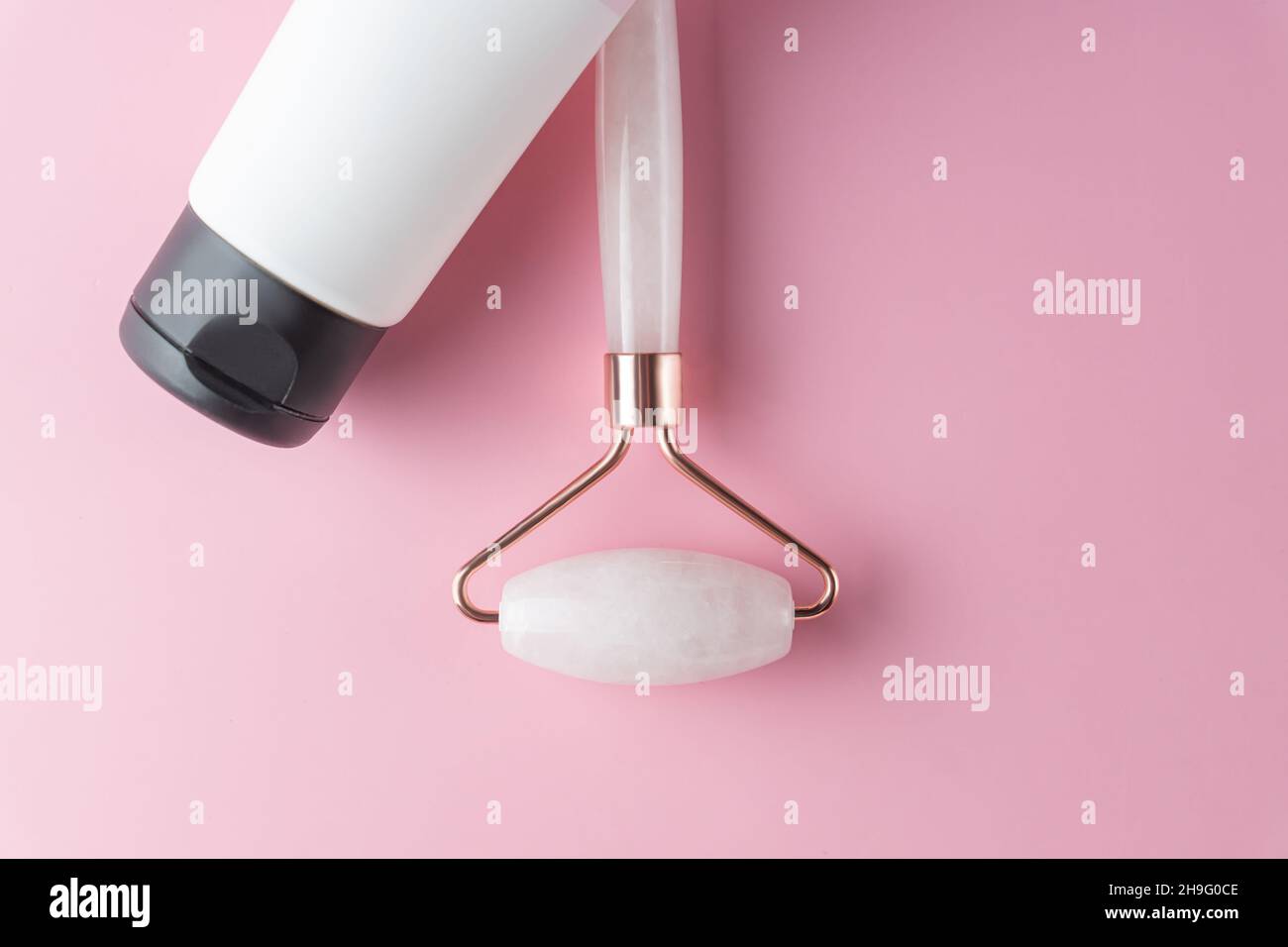 Beauty cosmetic facial roller, cream tube on pink background, top view ...