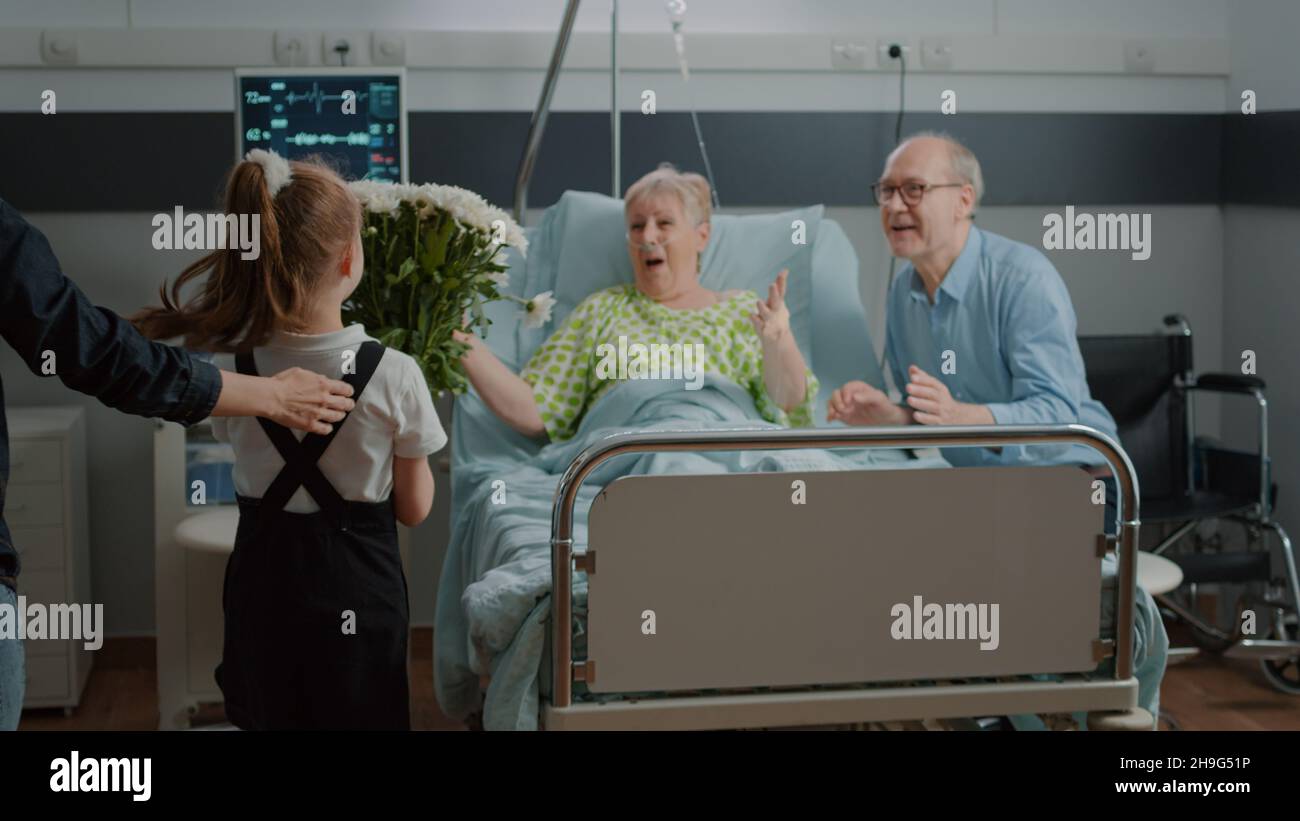 Little girl running to hug and give flowers to aged patient in hospital ...