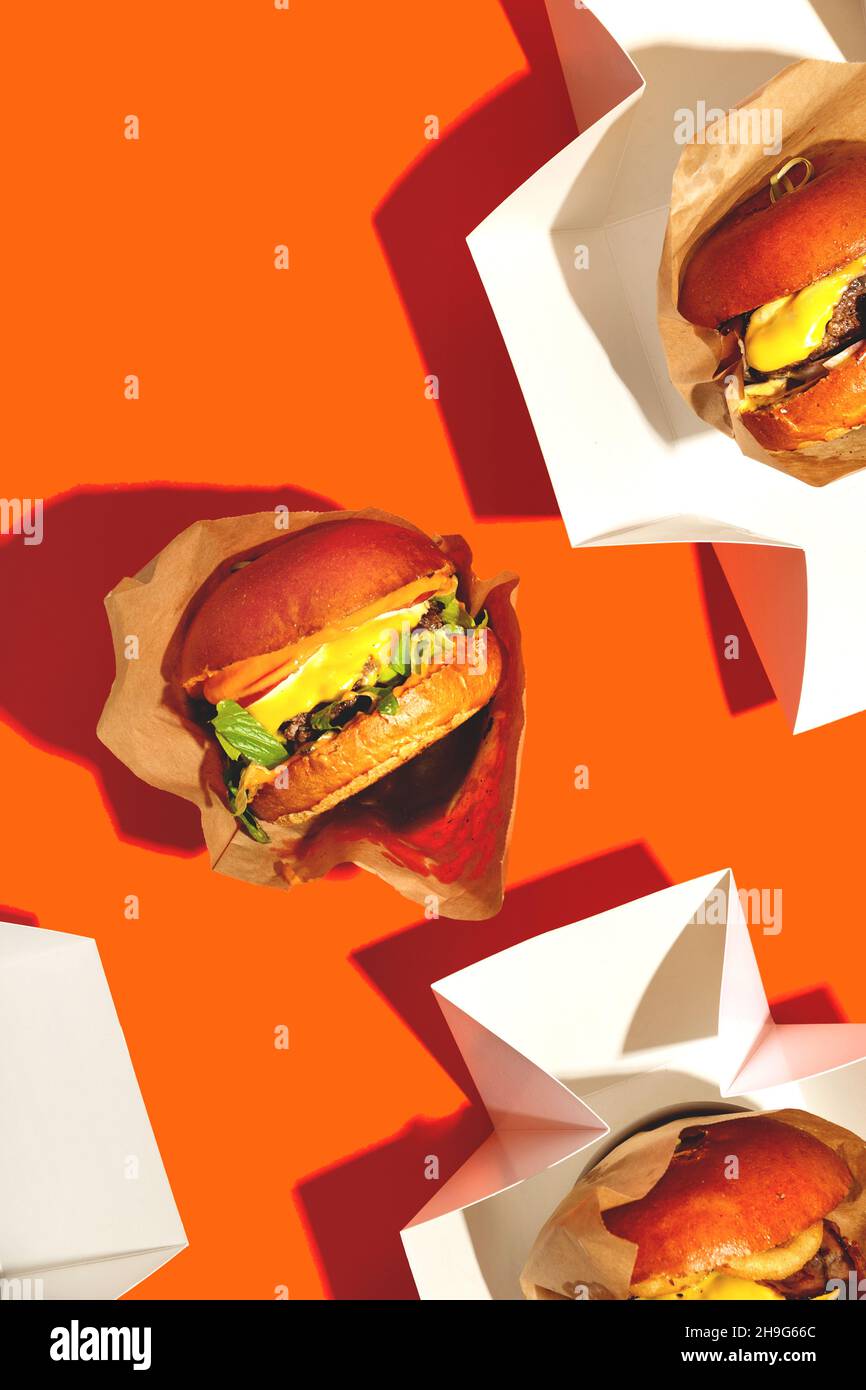 Big burger with cheese in a package on a bright orange background. Fast ...