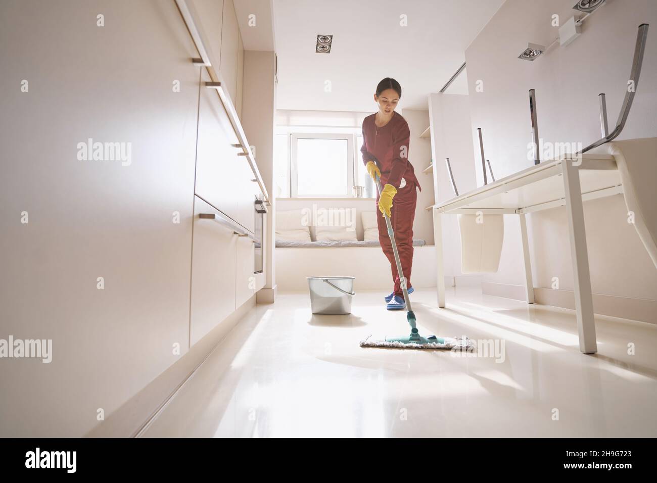 Full-length portrait of concentrated janitor cleaning floor with long ...