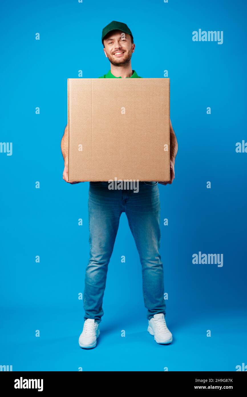 Delivery man with box in studio against blue background Stock Photo - Alamy