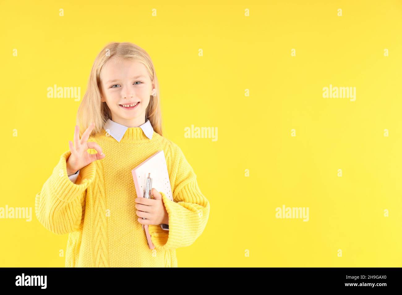 Cute little girl with notebook and pen on yellow background Stock Photo ...