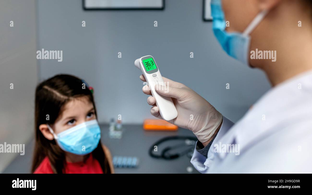 Female doctor looking at infrared thermometer after taking temperature ...