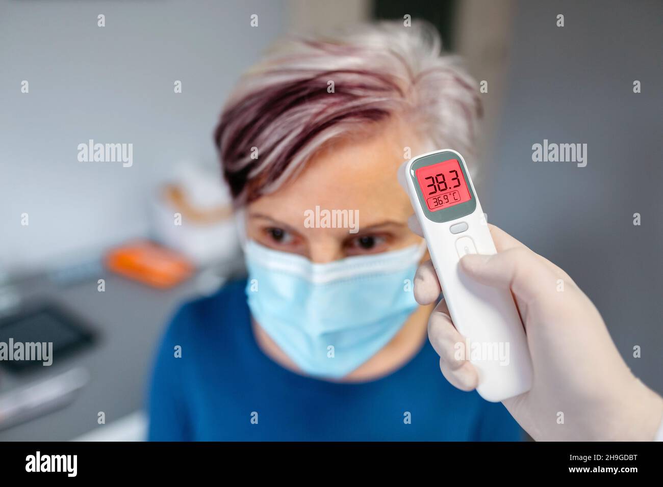 Senior woman with a fever whose temperature is taken by her female ...