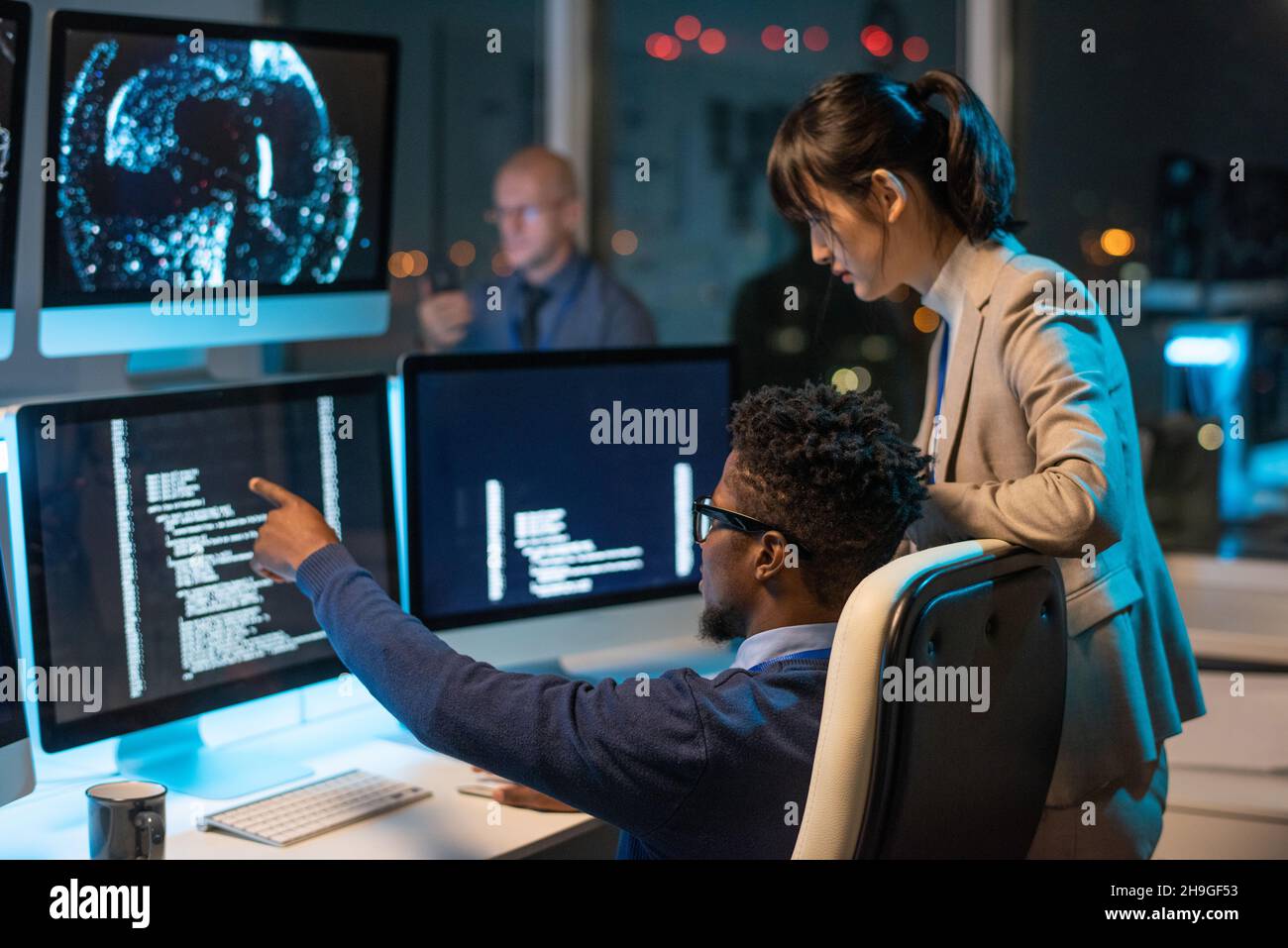 Confident businessman pointing at coded data on computer screen while explaining it to female ...