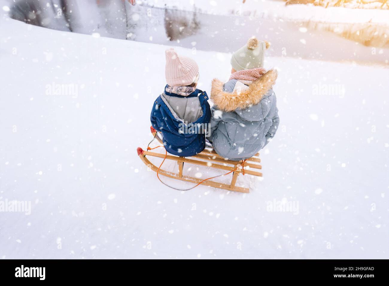 Two children ride on wooden retro sled on sunny winter day. Active ...