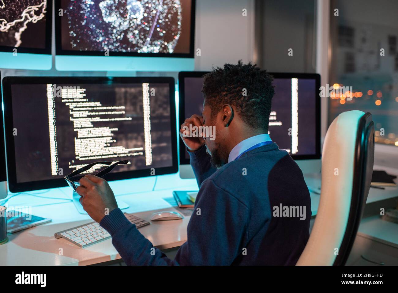 Young tired African businessman sitting in front of computer monitor ...