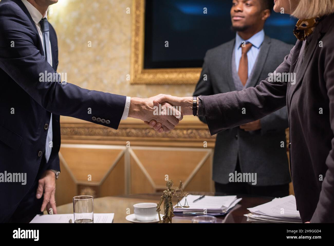 Handshake of successful business partners standing by table with documents against young African ...