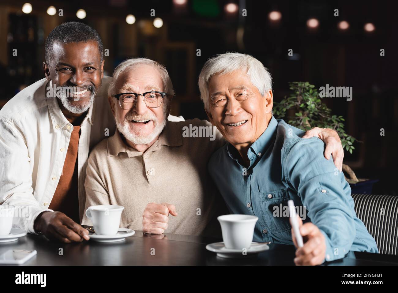senior multicultural friends embracing and smiling at camera near ...