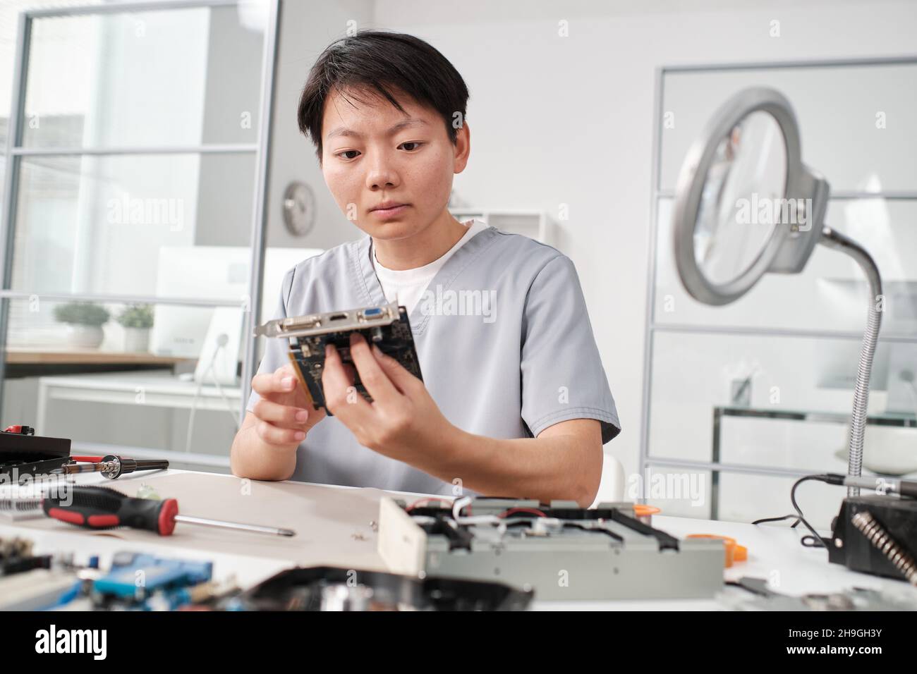 Young serious female specialist checking motherboard or part of ...