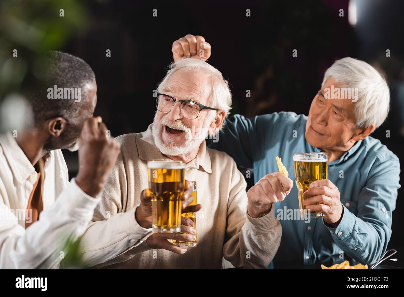 joyful, senior multiethnic men drinking beer while spending time in pub ...