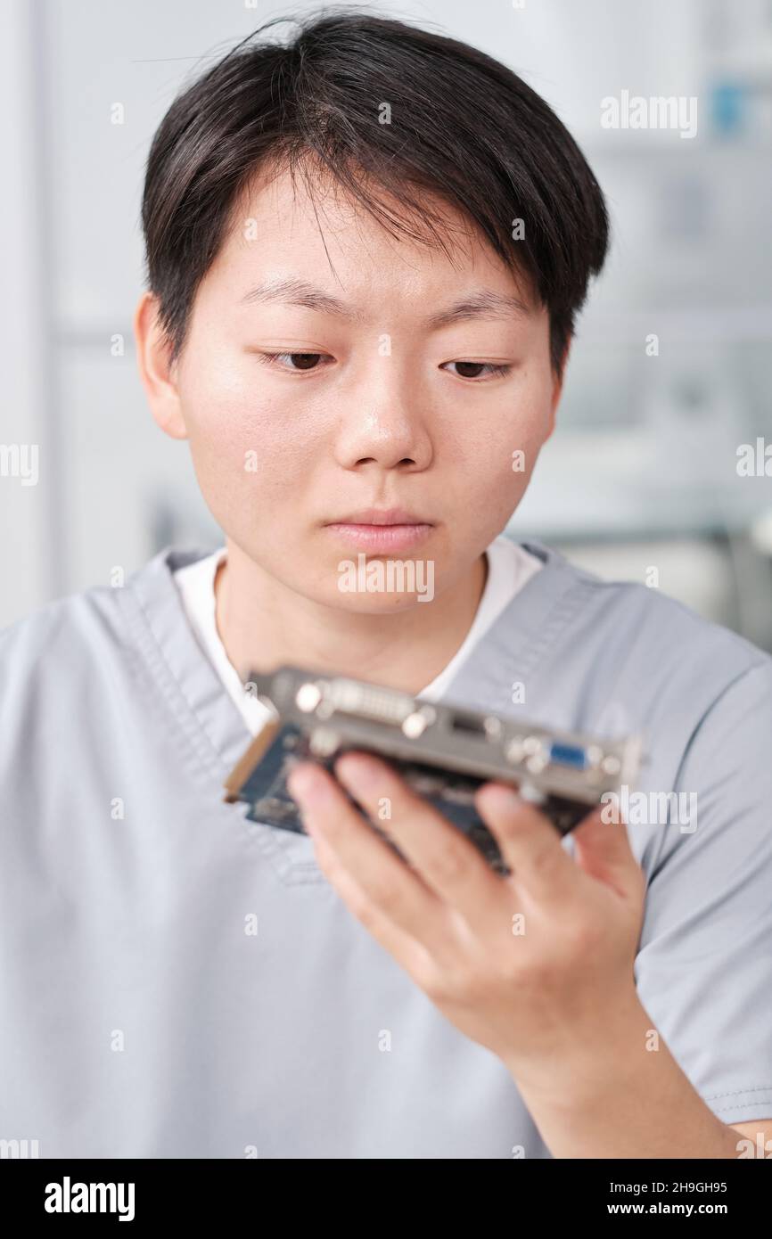 Serious female technician looking at hardware in her hand while ...