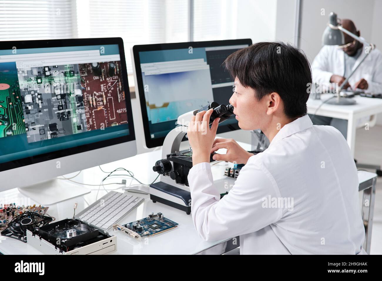 Young contemporary researcher with microscope looking at computer ...