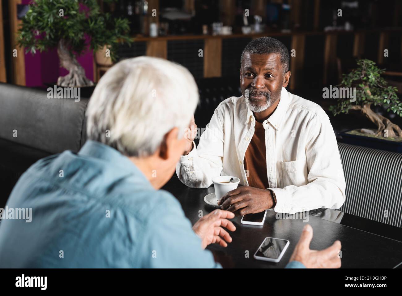 senior african man talking to blurred friend during meeting in bar ...
