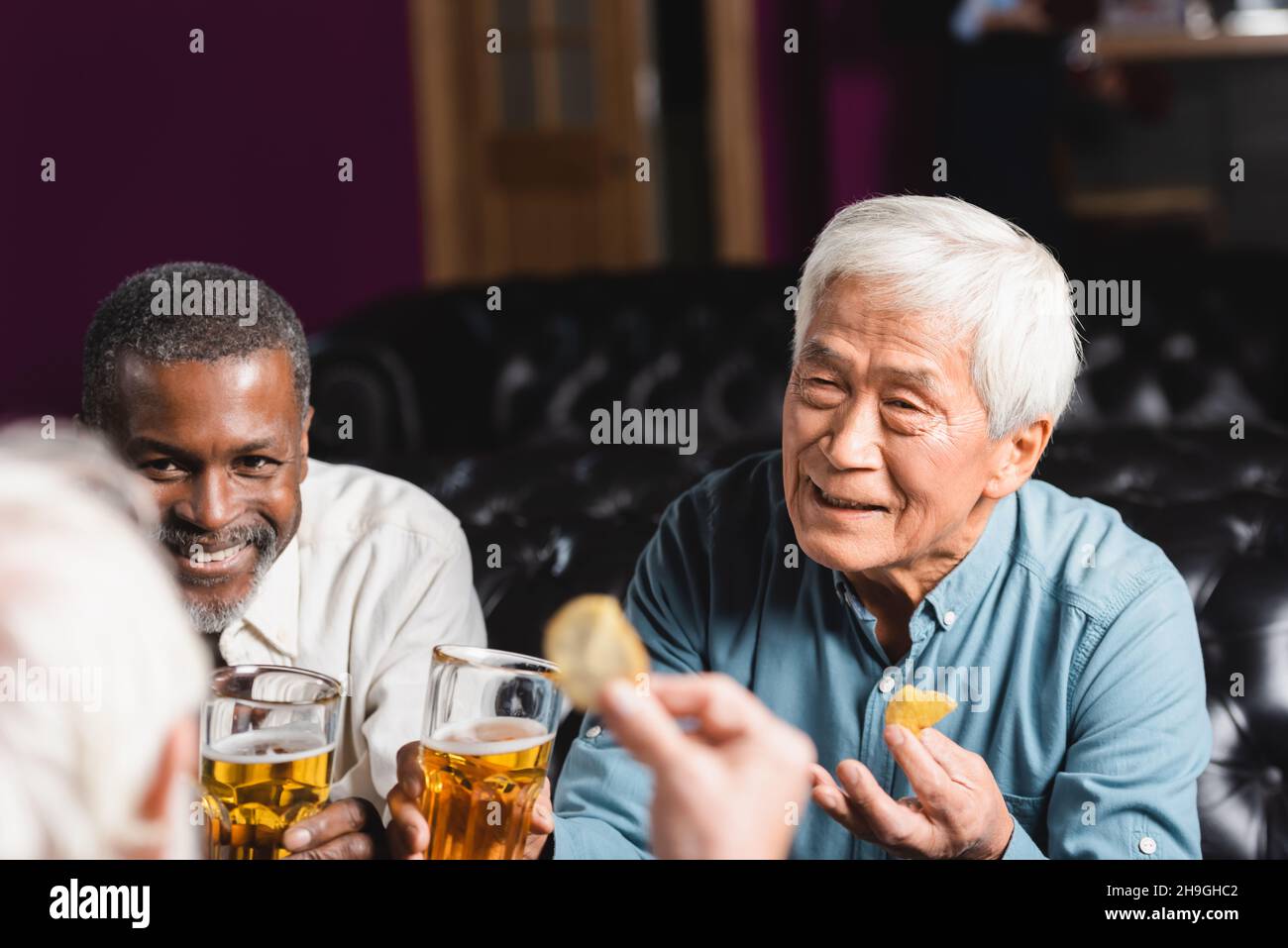 senior multicultural friends talking, drinking beer and eating chips in ...