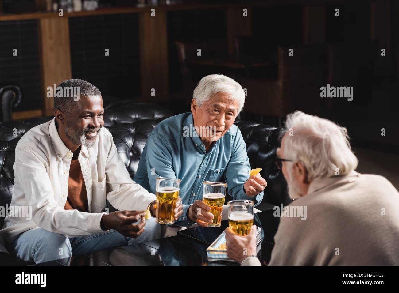 senior multicultural friends holding glasses of beer while spending ...