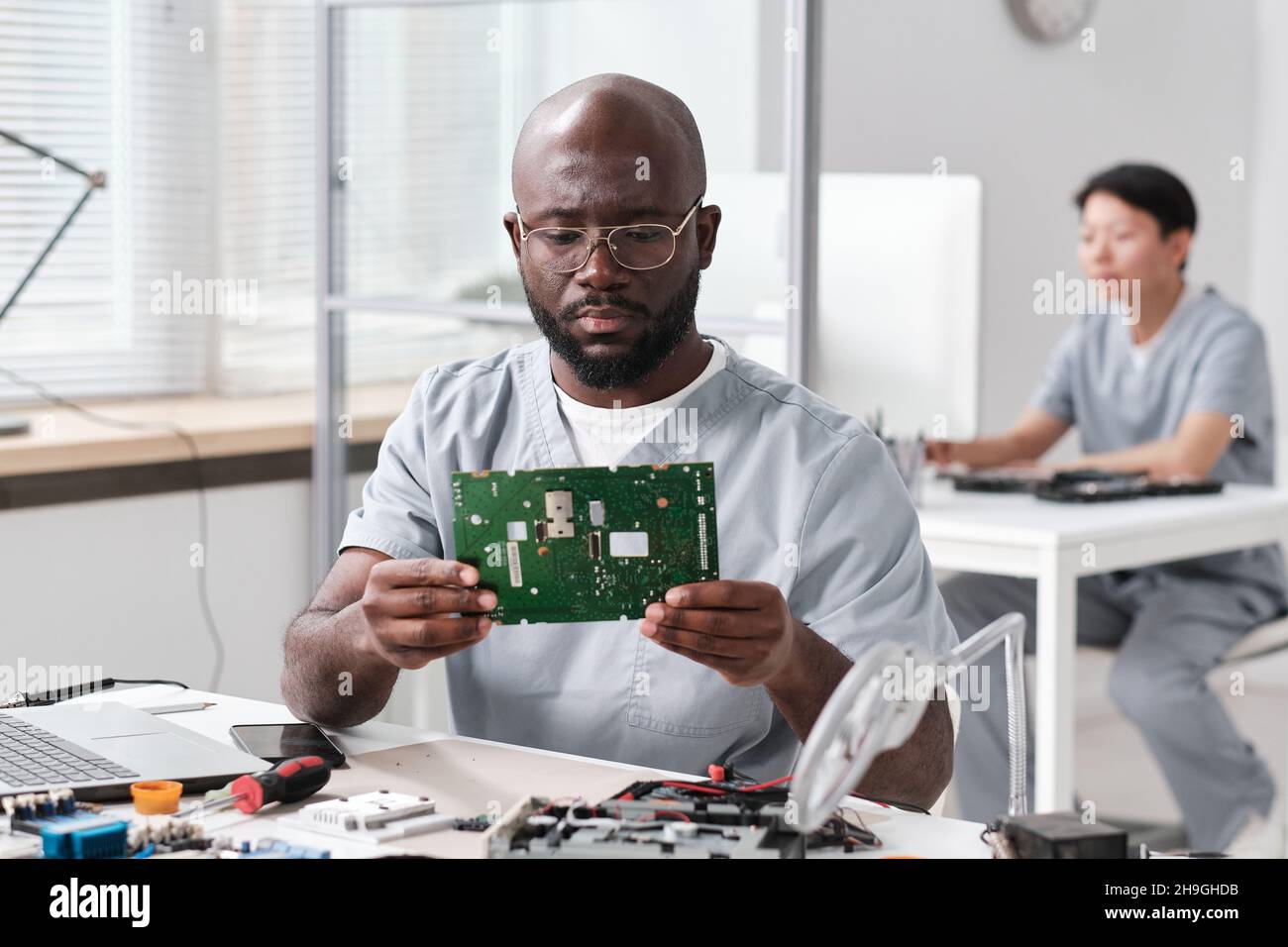 Serious African man in workwear looking at motherboard in hands while ...