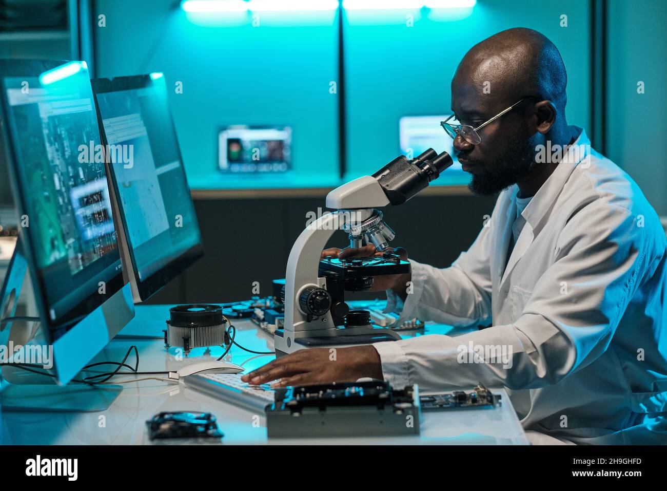 Young African researcher with microscope pressing key of computer ...
