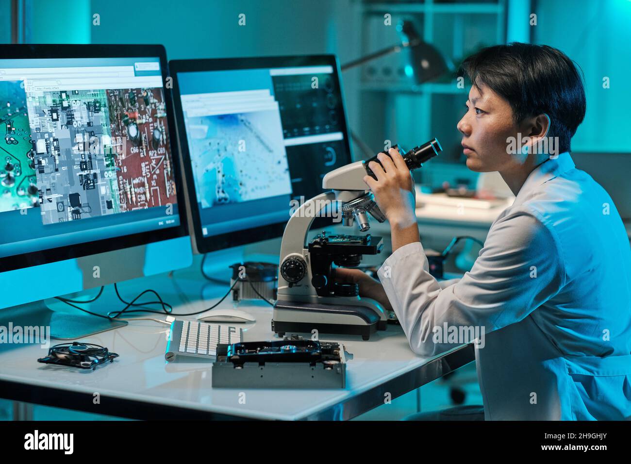 Young serious female scientist with microscope looking at computer ...