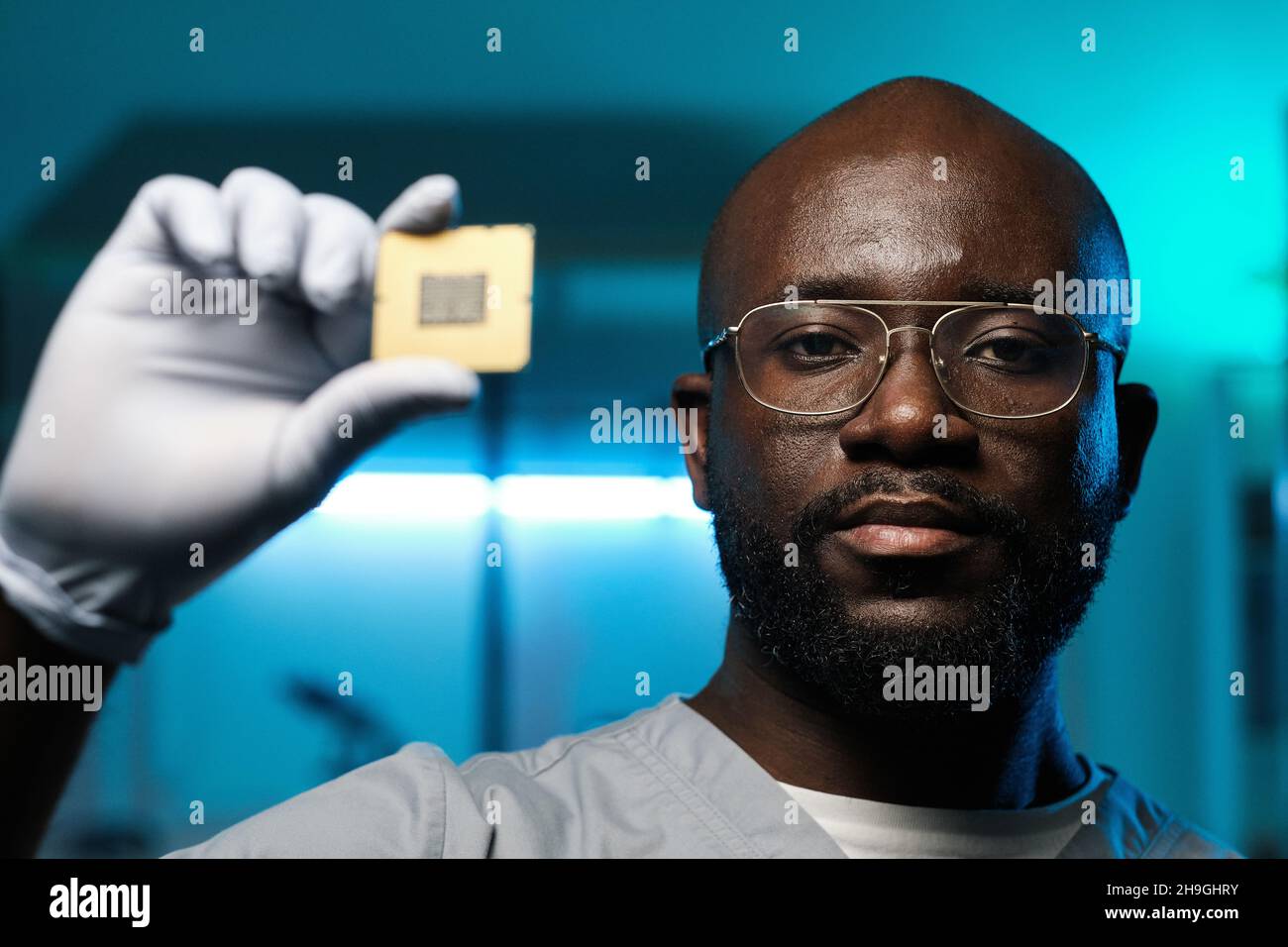 Young serious man of African ethnicity holding microchip in gloved hand ...