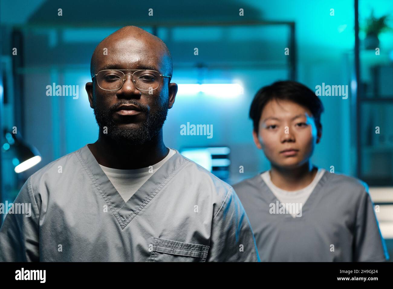 Two young intercultural researchers in uniform looking at camera while ...