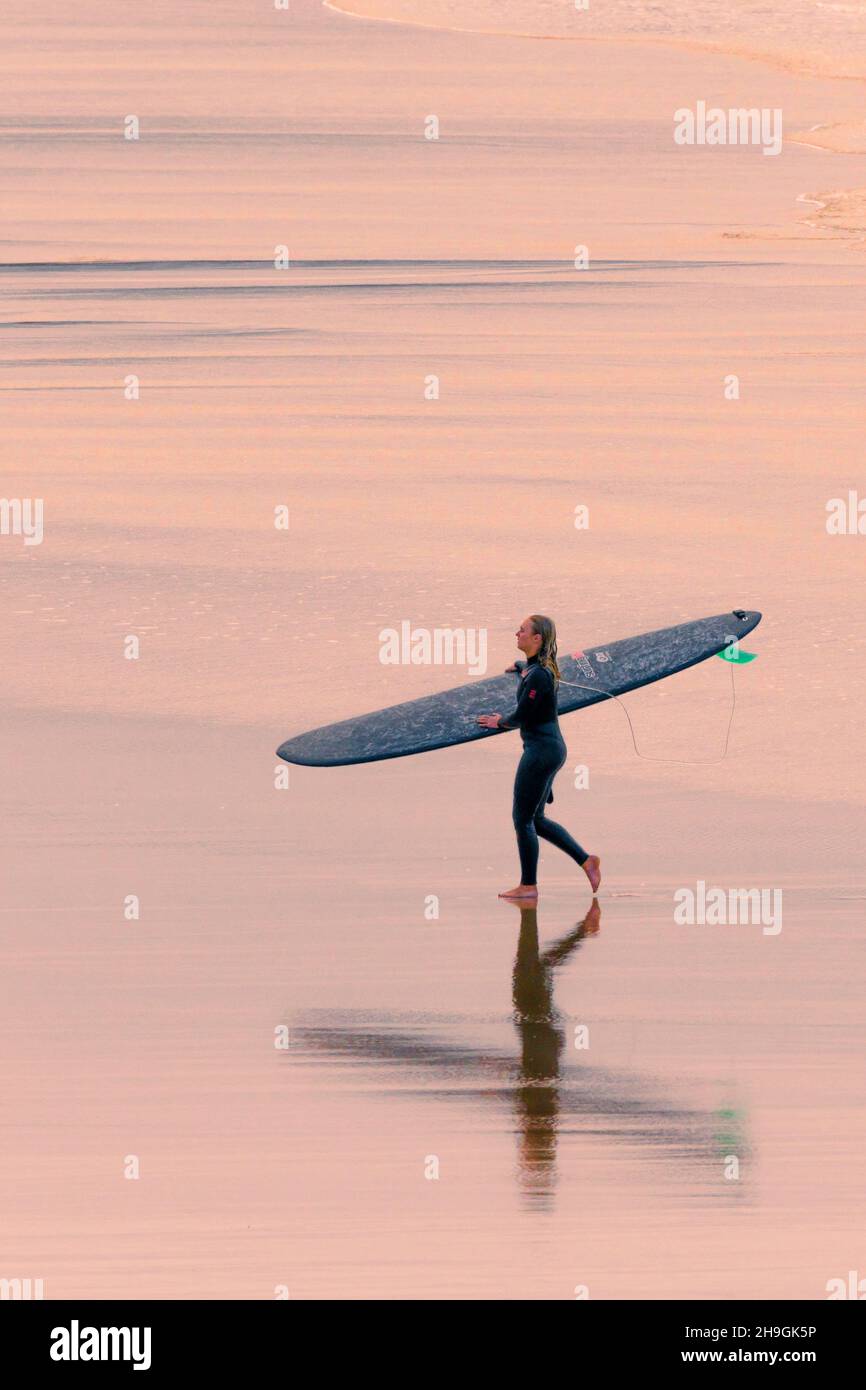 Warm evening light over a female surfer carrying his surfboard and ...