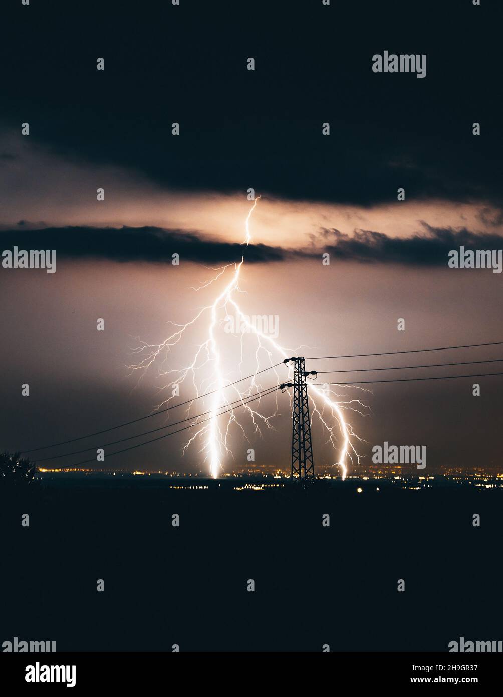 Long, branched, powerful lightning bolts strike down behind the trees ...