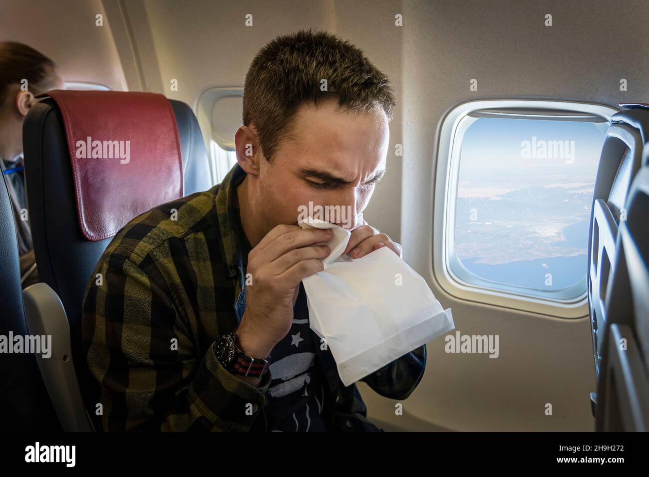 Nervous young man with aviophobia breathing into paper bag in airplane ...