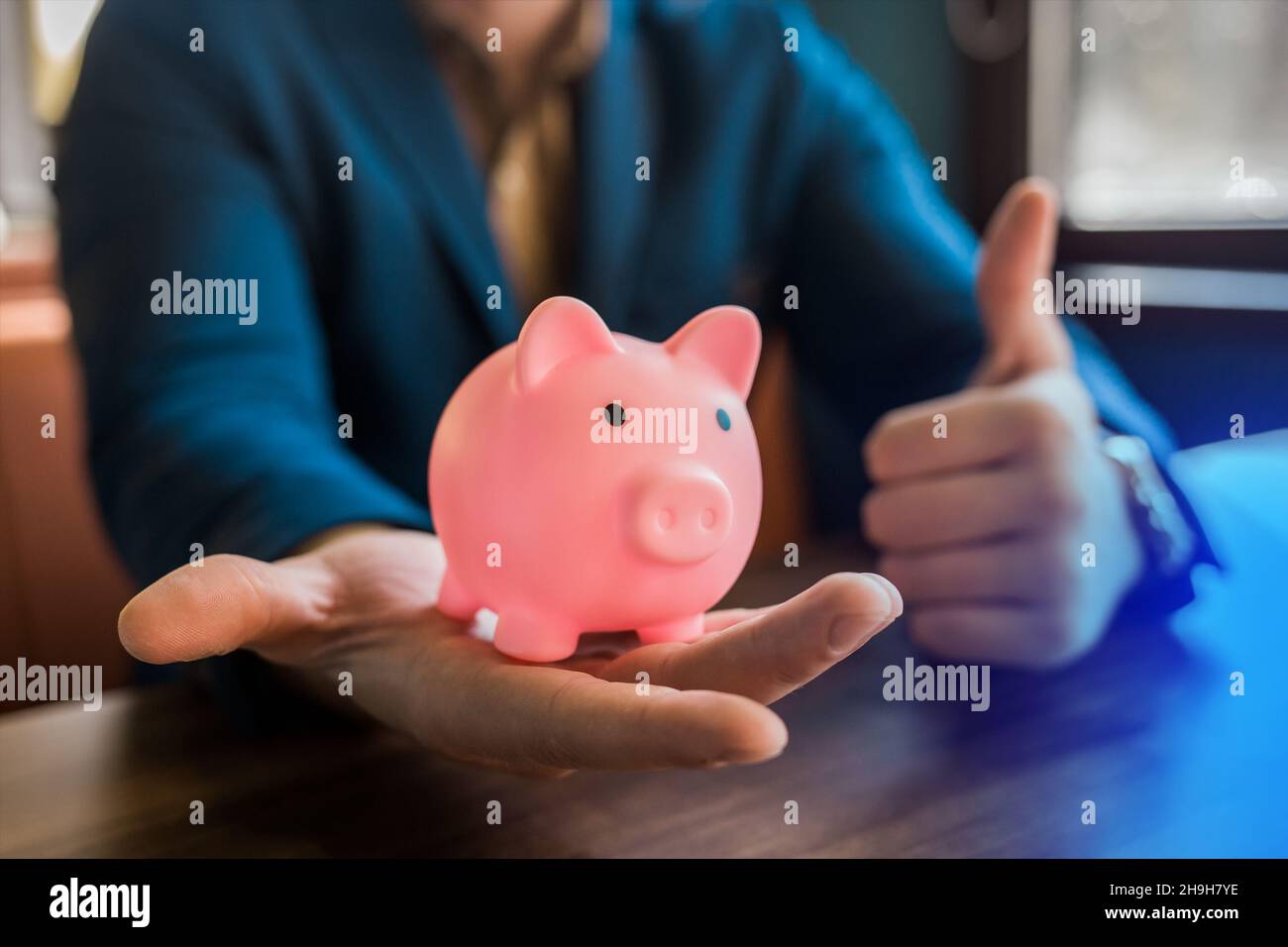 A businessman's hand holds a piggy bank of a means to save money, and ...