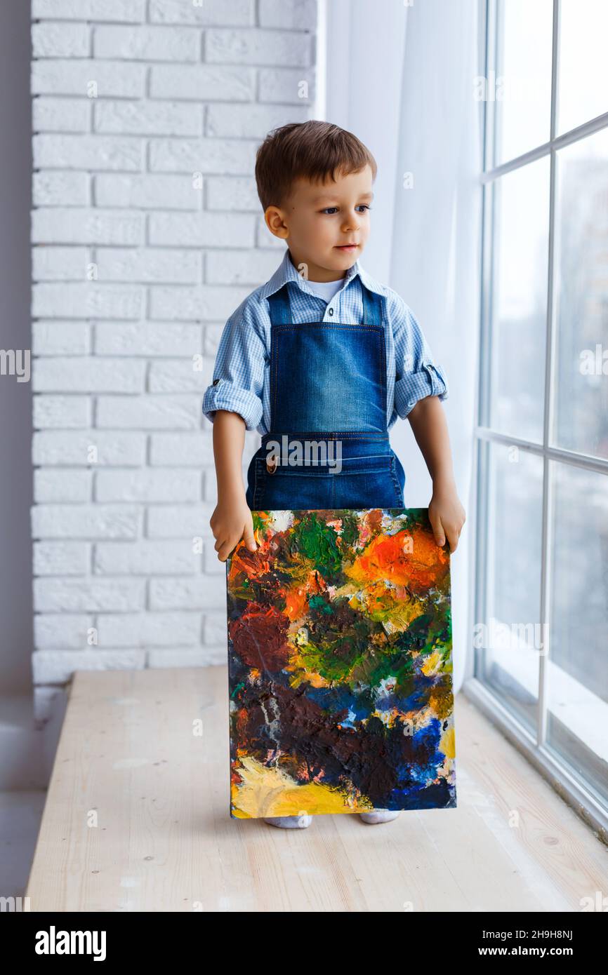 Cute, happy, white boy in blue shirt and jeans sitting near window with ...