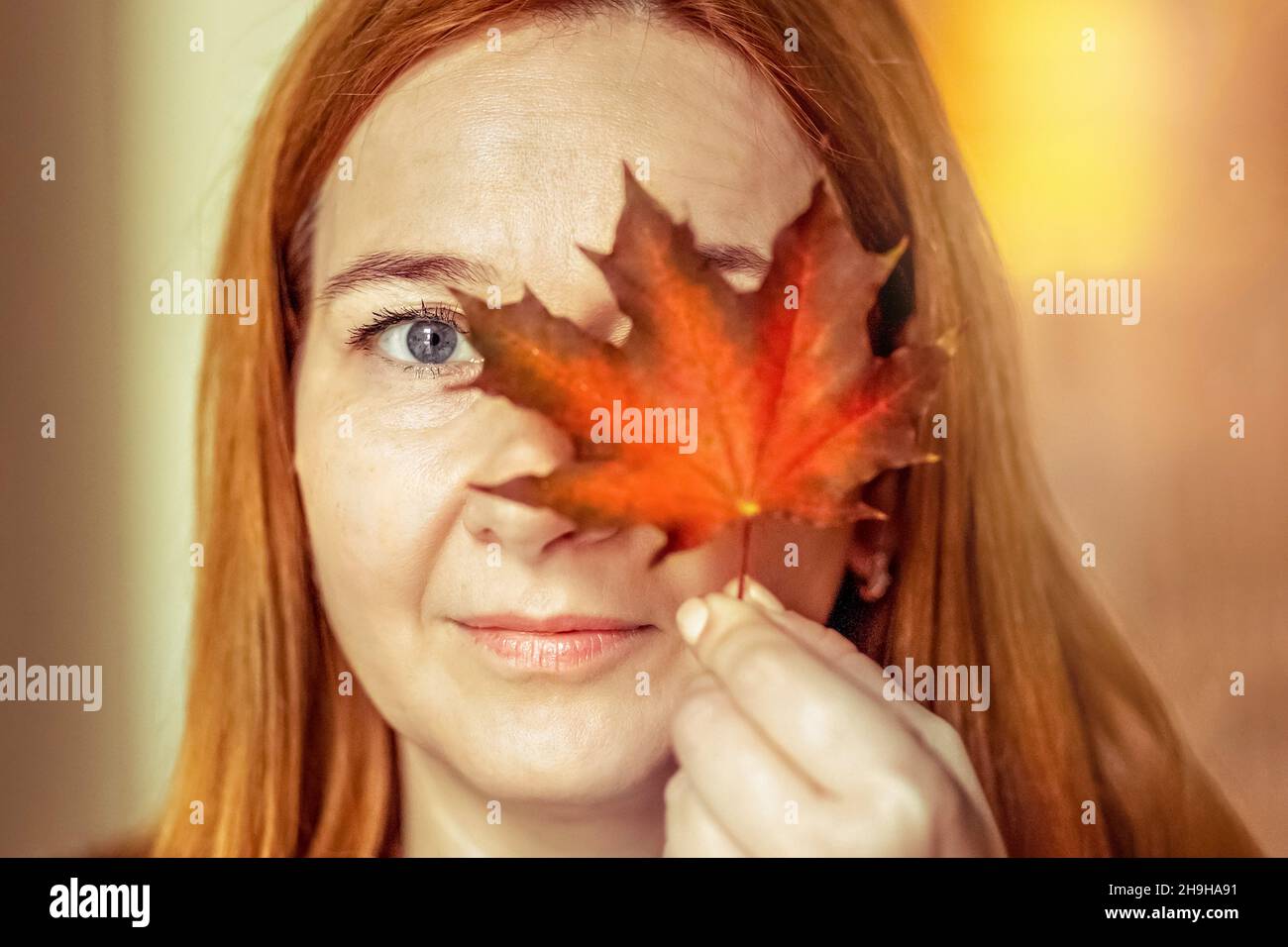 Portrait of a young woman covering one eye with an autumn fallen maple ...