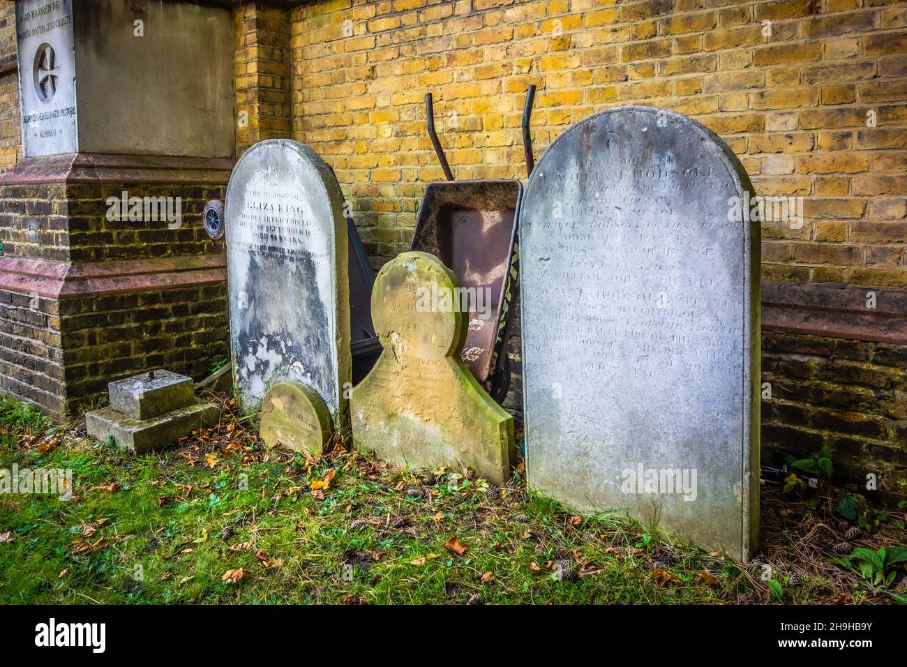 Grave stones against a brick wall of a church with a wheelbarrow ...