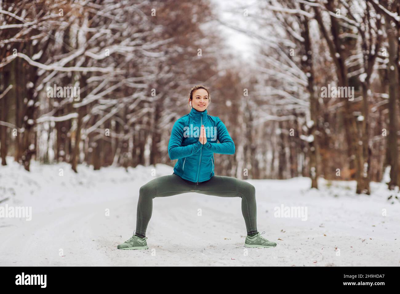 Fit sportswoman in sportswear doing yoga exercises in snowy forrest ...