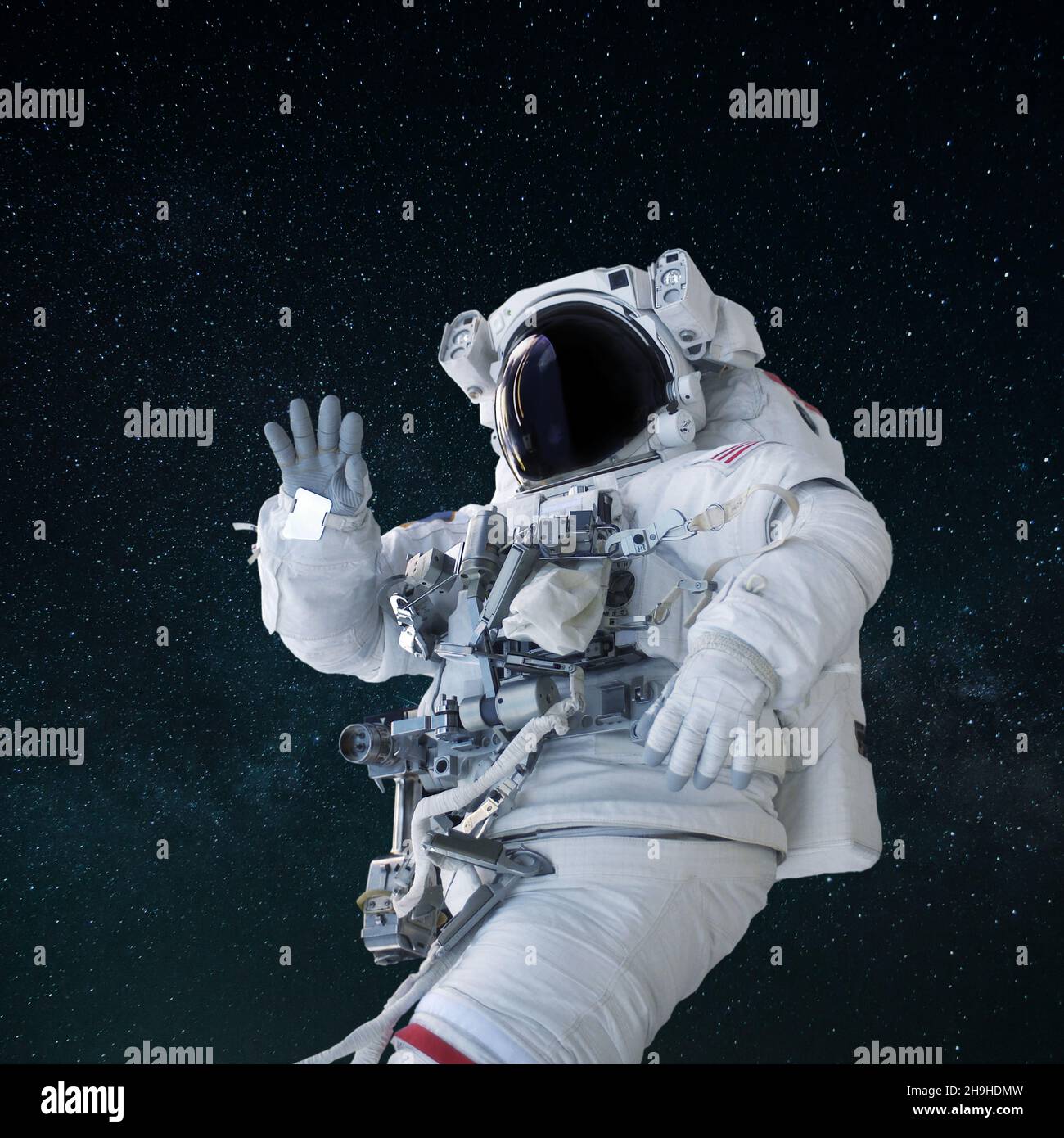 Space man in a suit with a helmet waves his hand and greeting in open ...