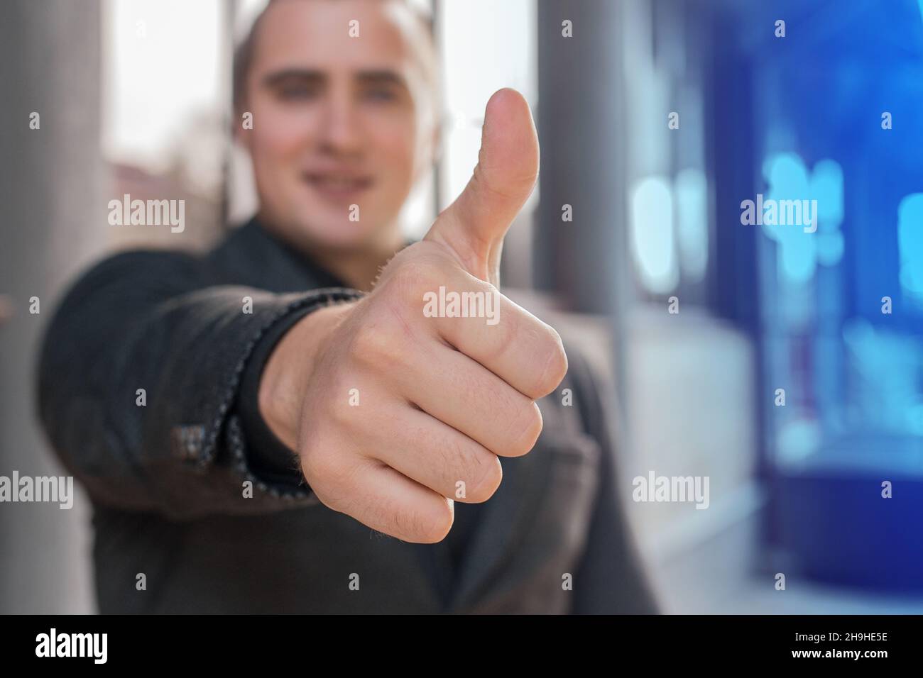 A young man shows a close-up of a thumbs up class against a street ...