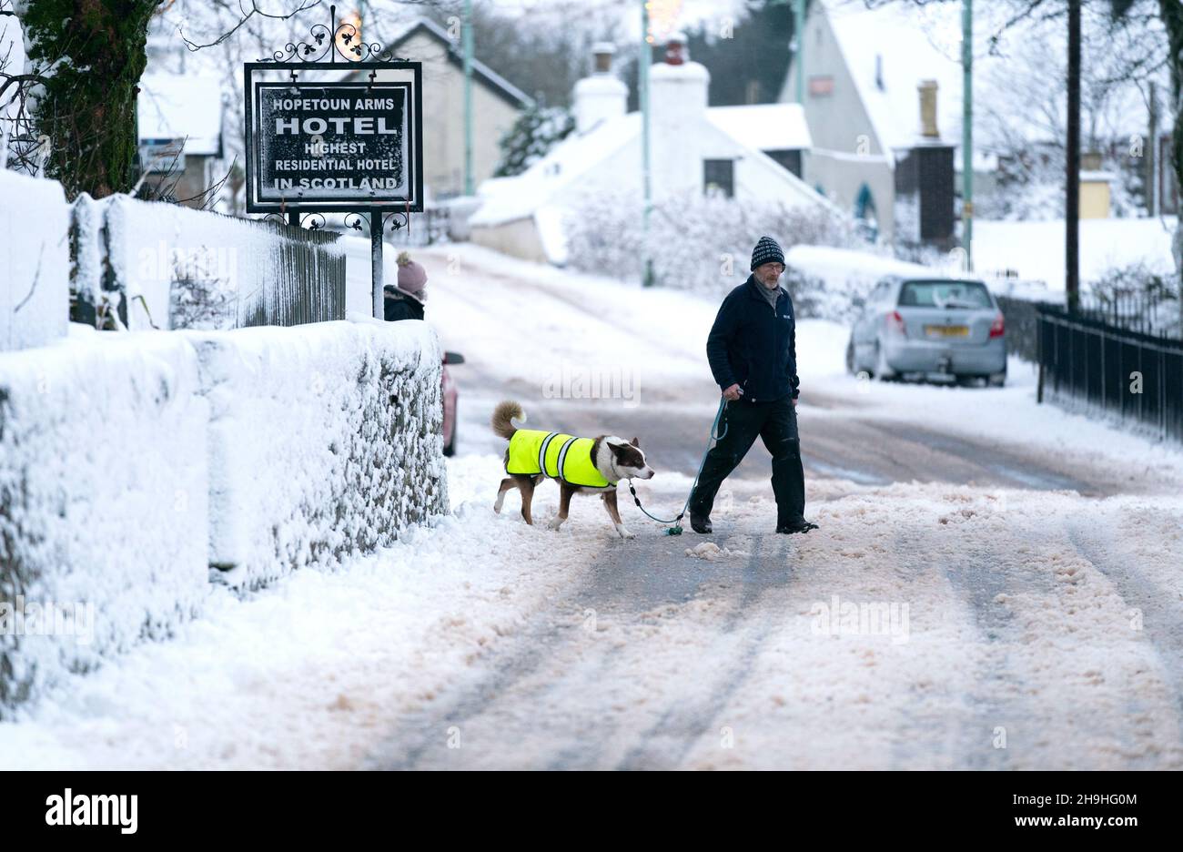 A man walks his dog through the snow in Leadhills, South Lanarkshire as ...