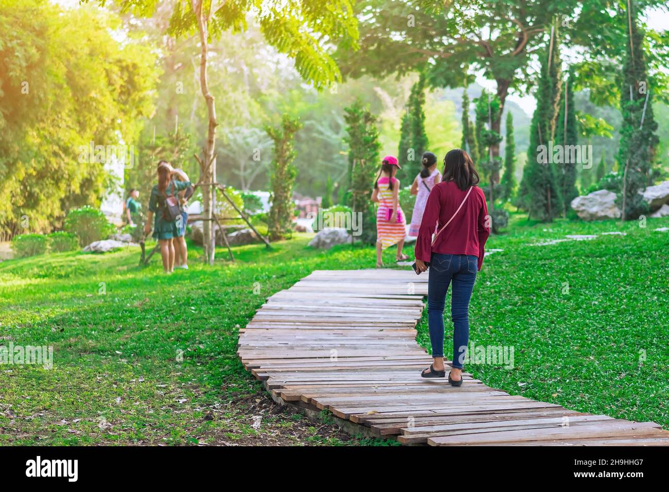 Back view of Asian woman walk alone on pathway through green garden ...