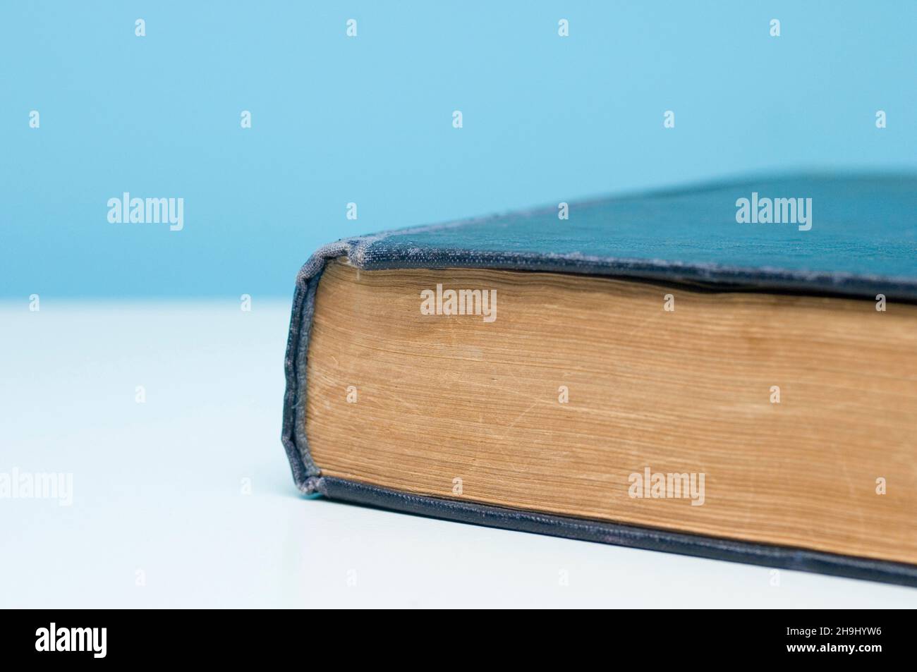 Old book laying at an angle on a white surface against an aqua blue ...