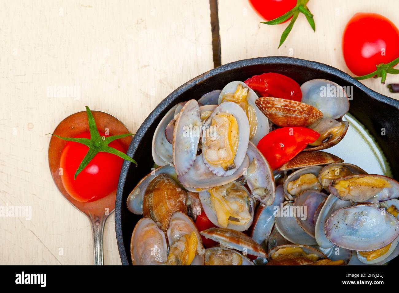 fresh clams stewed on an iron skillet over wite rustic wood table Stock ...