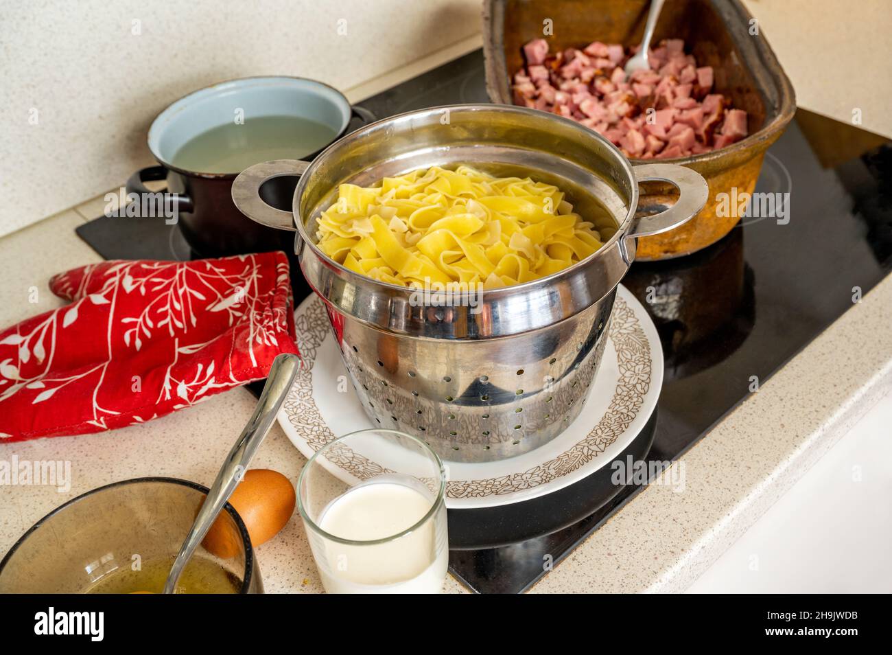Colander with boiled wide pasta,egg, milk, red potholder, earthenware ...