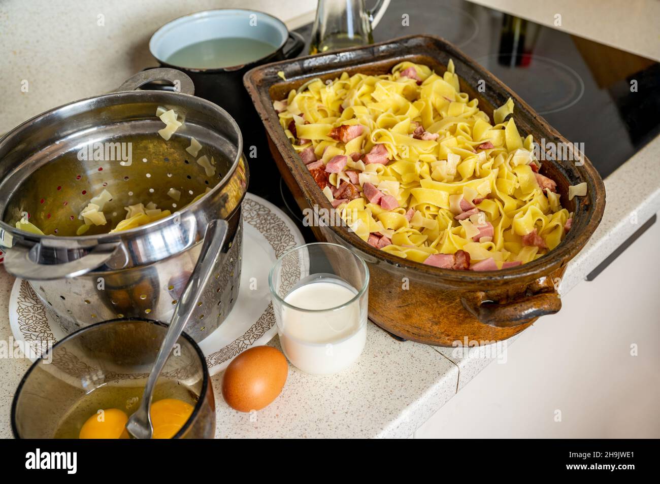 Earthenware baking pan with pasta and smoked meat, milk, egg, pot and ...