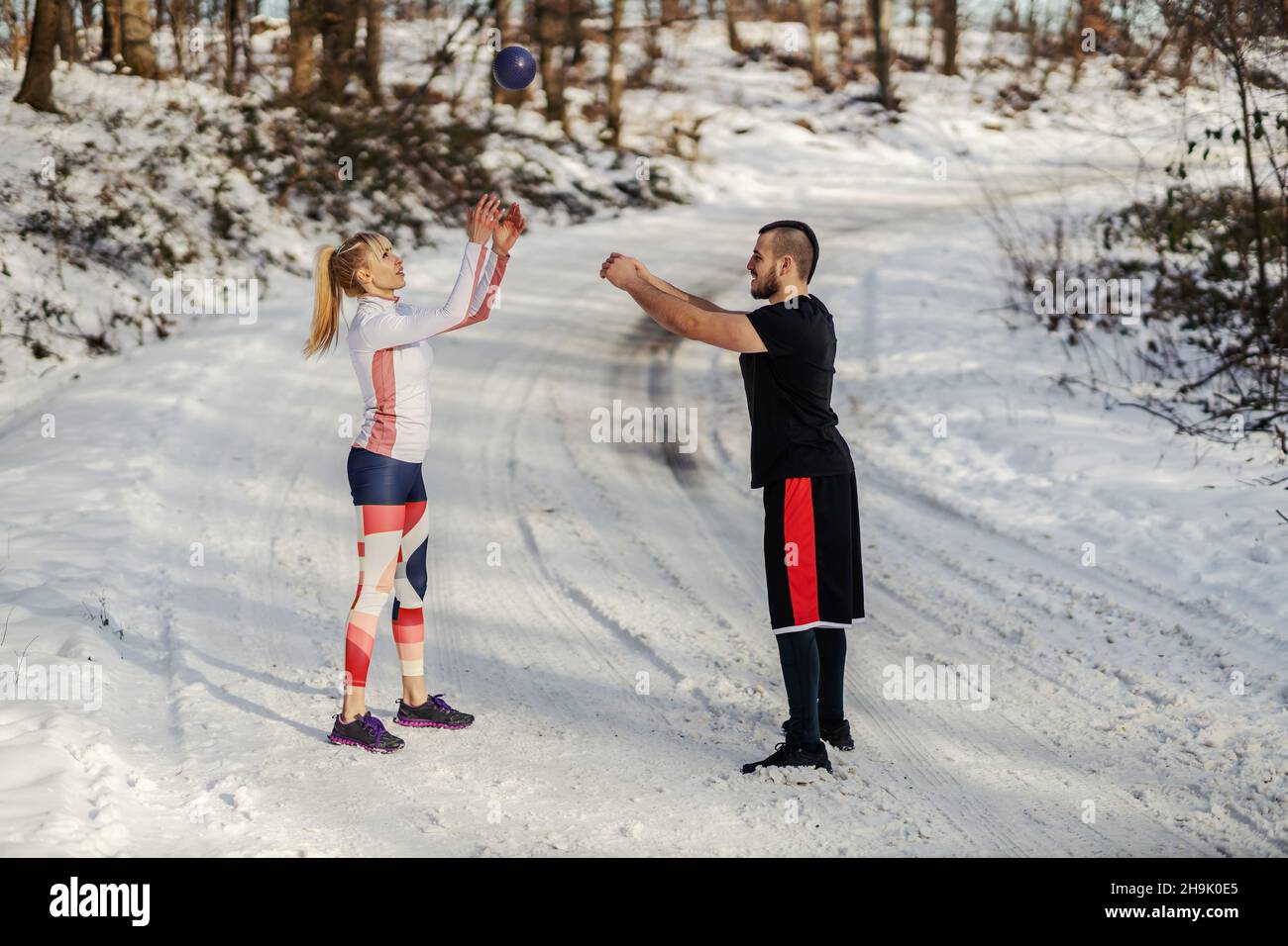 Sporty couple standing in snow in nature and doing warm up exercises ...