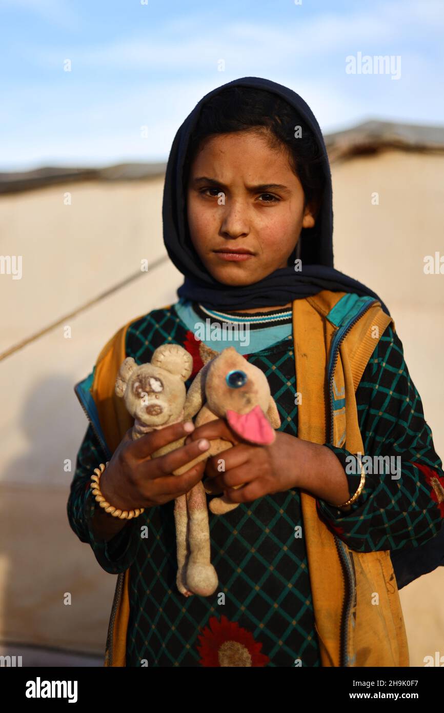 A Syrian little girl named Millions, stands beside her tent holding ...