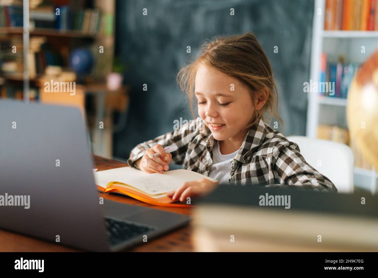 Cheerful positive primary child school girl doing homework writing ...
